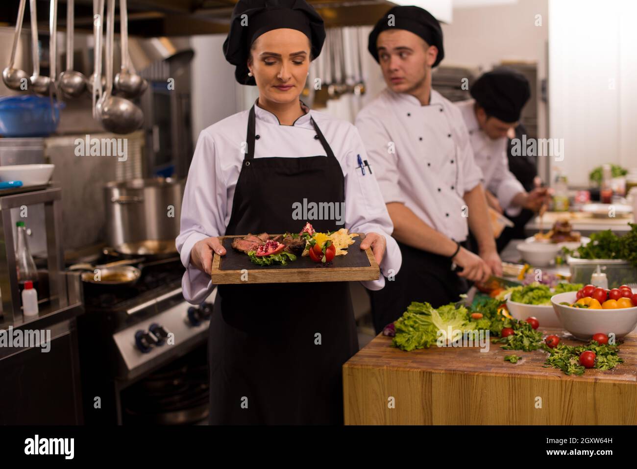 female Chef in hotel or restaurant kitchen holding grilled beef steak ...