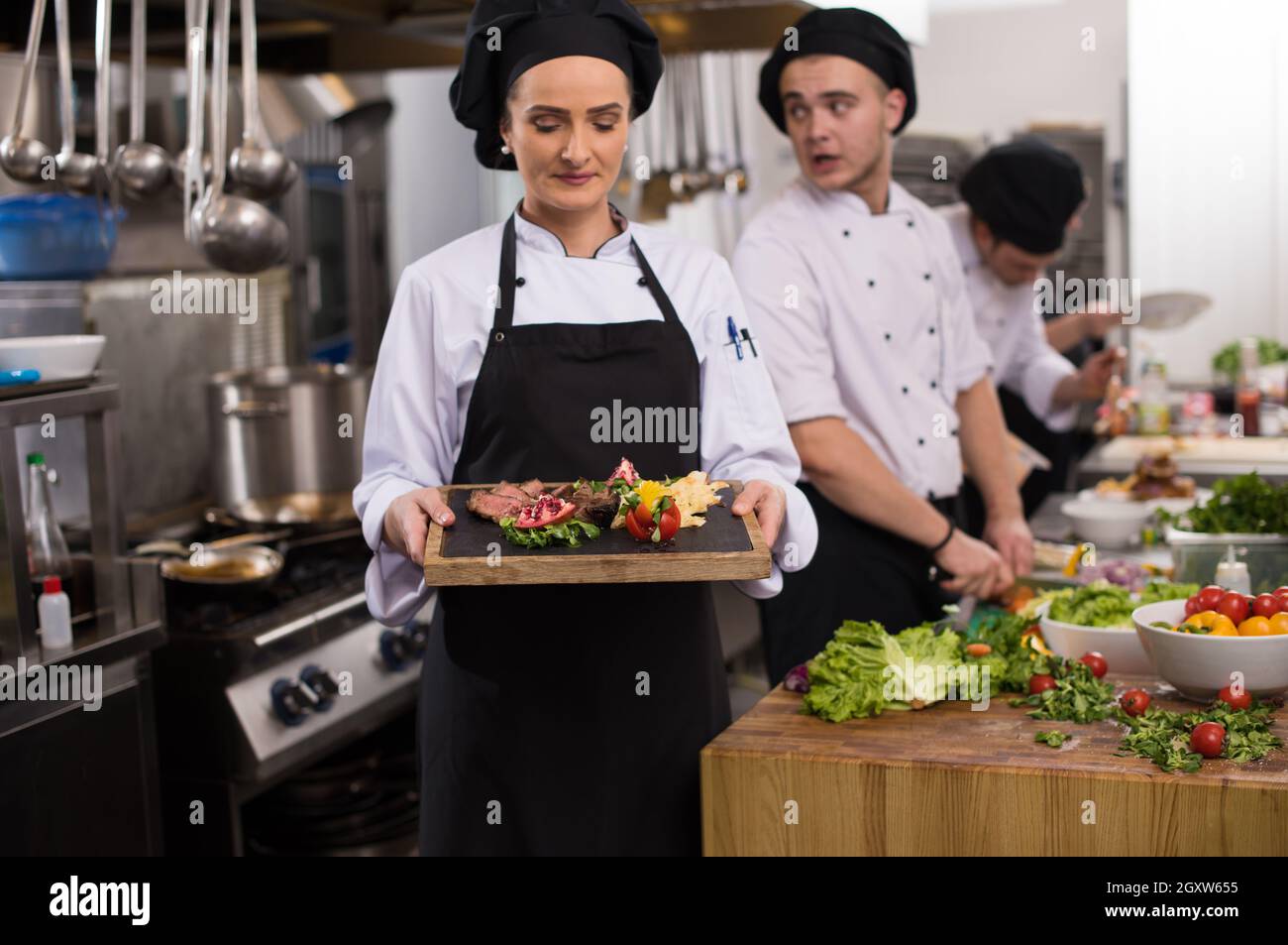 female Chef in hotel or restaurant kitchen holding grilled beef steak ...