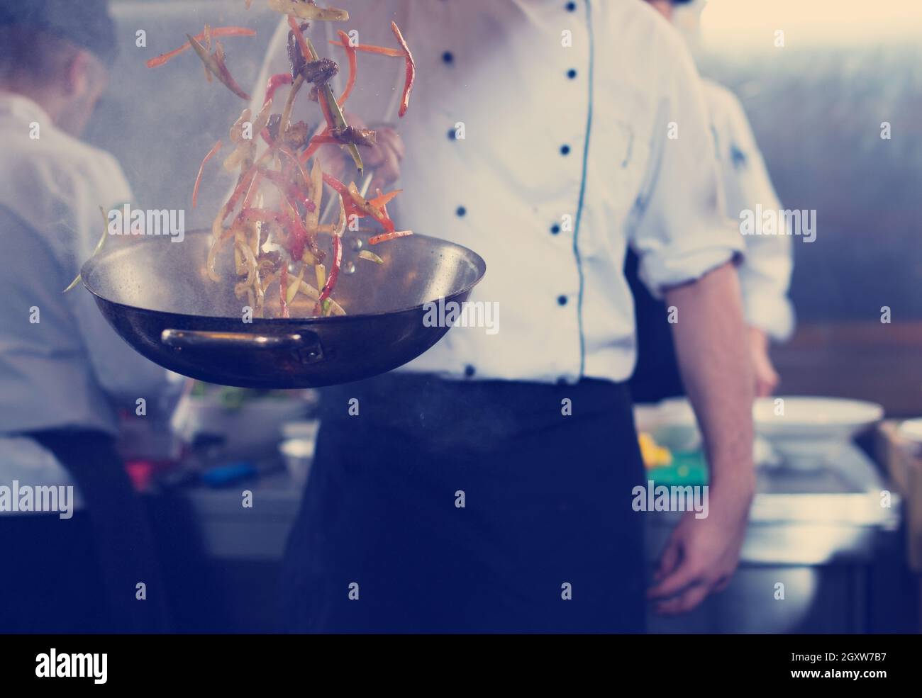 Young male chef flipping vegetables in wok at commercial kitchen Stock ...