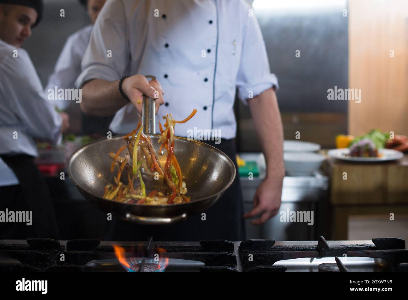 Young male chef flipping vegetables in wok at commercial kitchen Stock ...