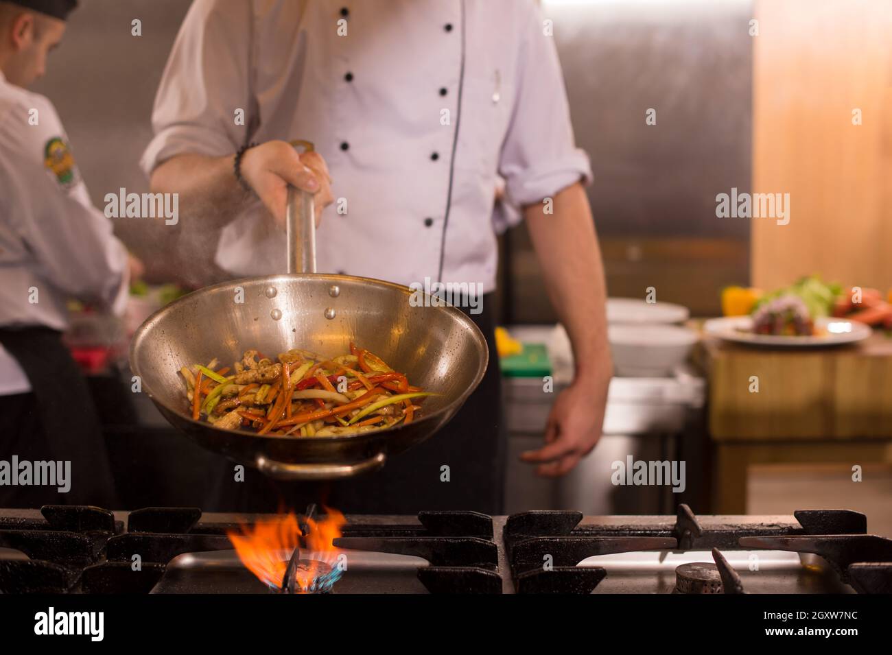 Young male chef flipping vegetables in wok at commercial kitchen Stock ...