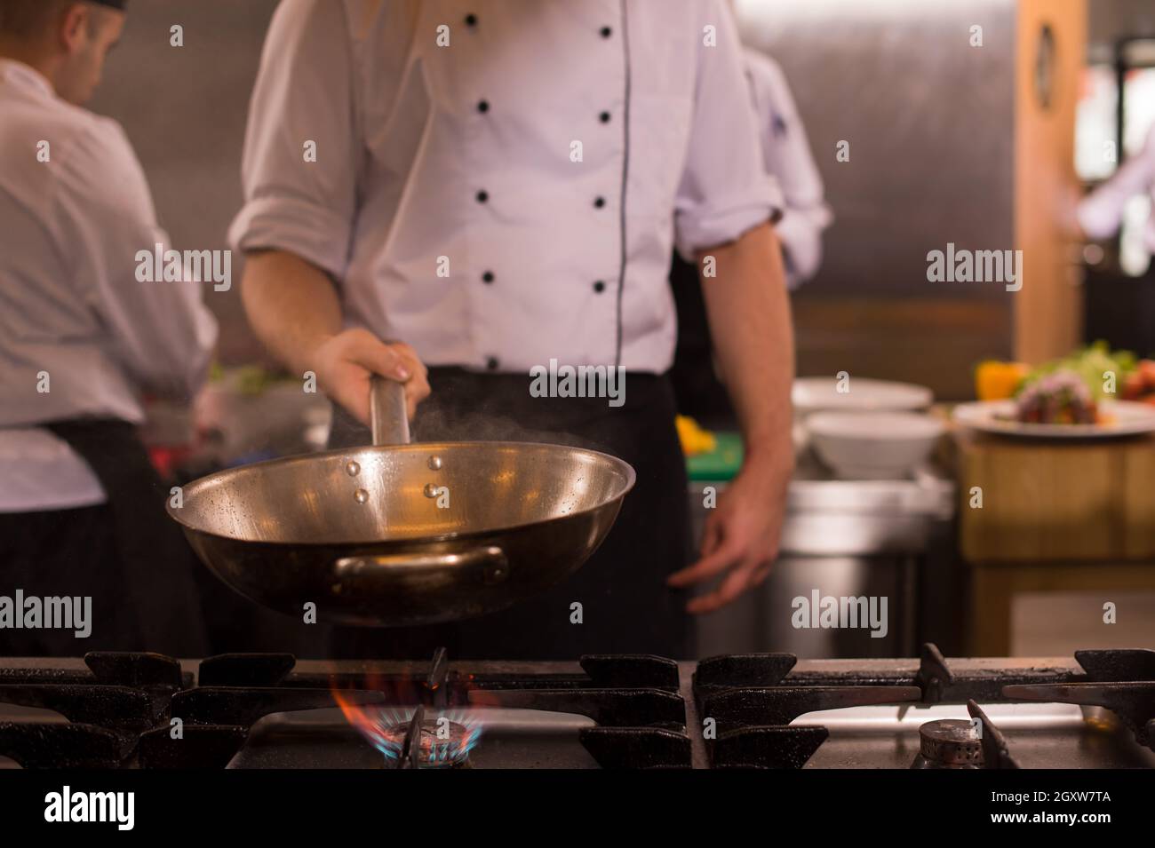 Young male chef flipping vegetables in wok at commercial kitchen Stock ...