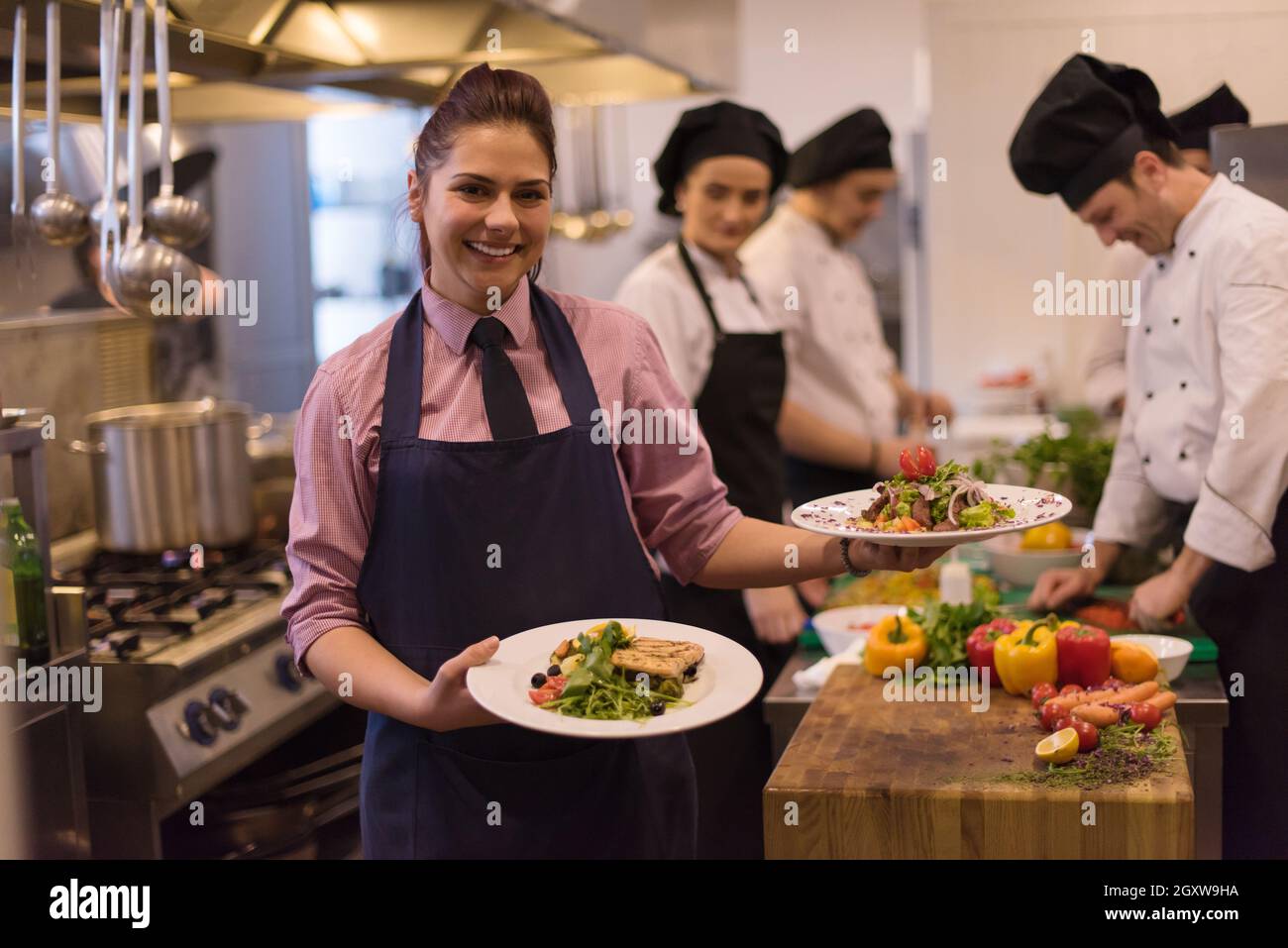 young waitress presenting dishes of tasty meals in commercial kitchen ...