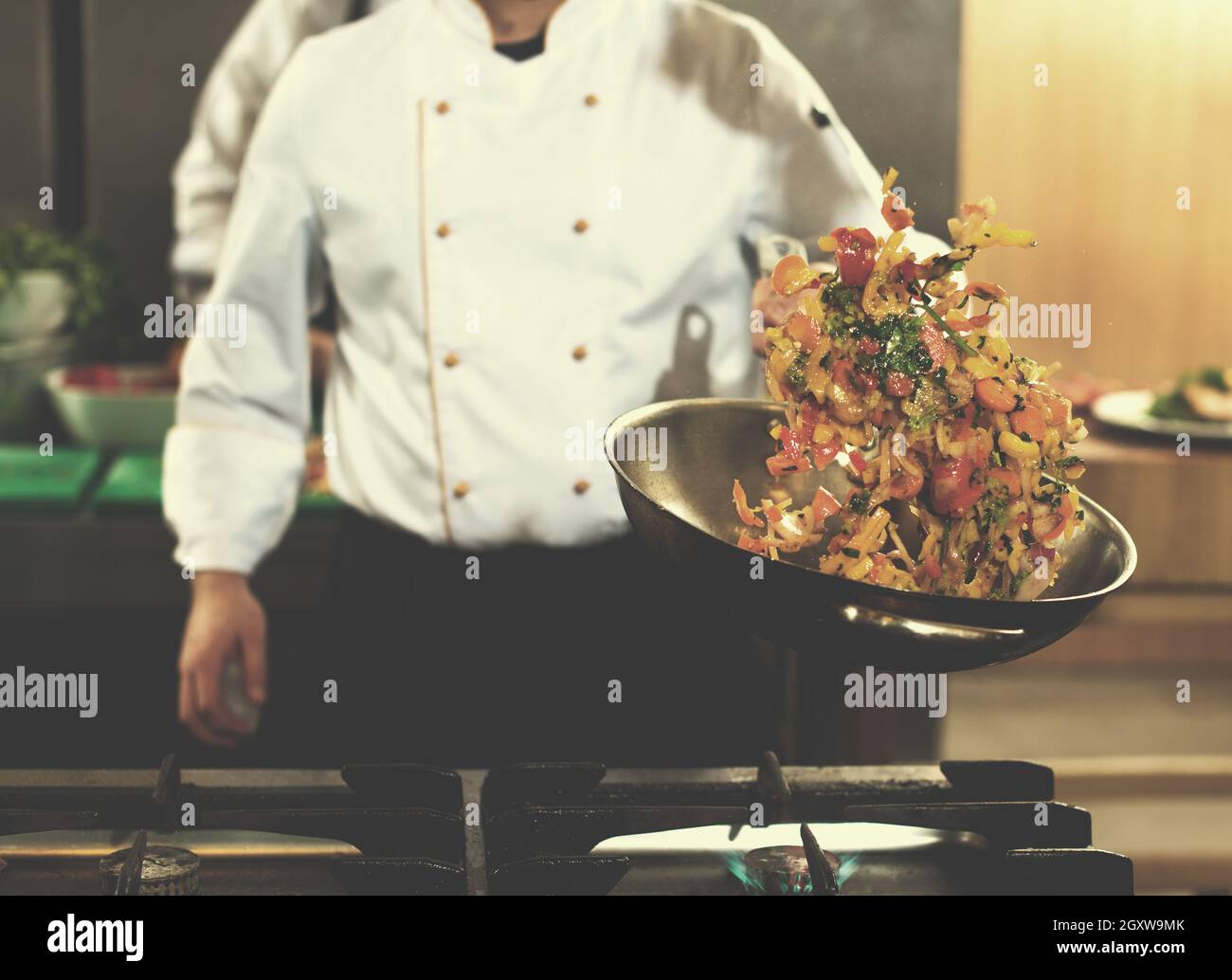 Young male chef flipping vegetables in wok at commercial kitchen Stock ...