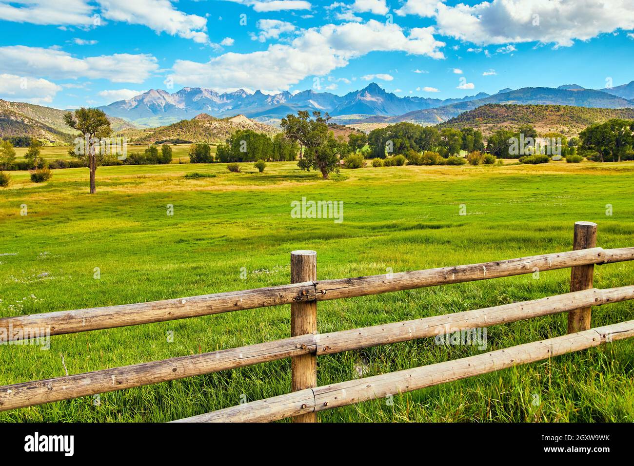 Landscape of wood fence, open green field, and background of majestic ...