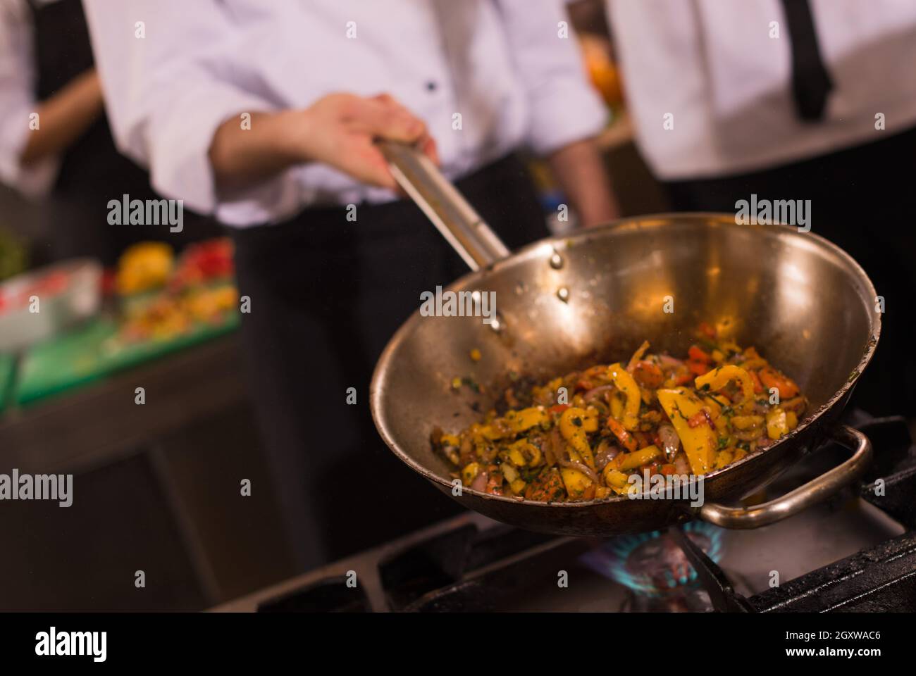 Young male chef flipping vegetables in wok at commercial kitchen Stock ...