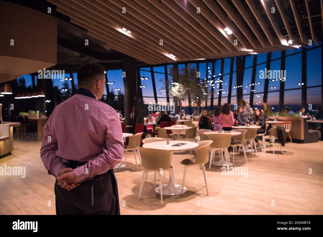 Rear view of young confident waiter standing with hands behind his back ...