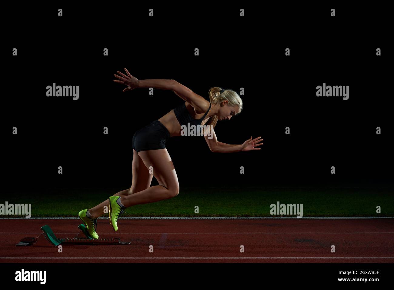 woman sprinter leaving starting blocks on the athletic track. Side view ...
