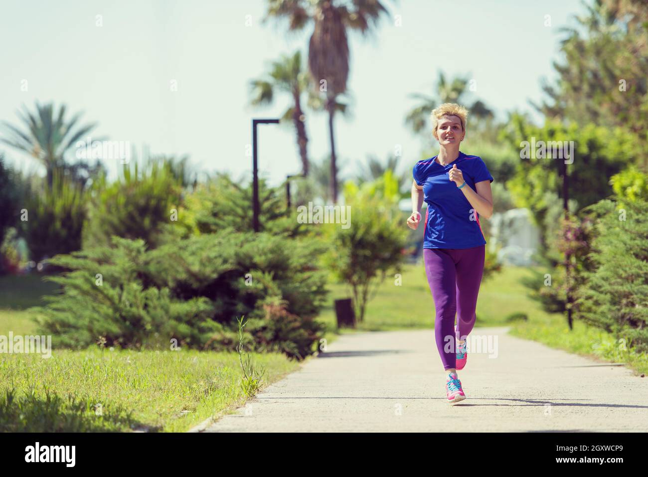 young sporty female runner training for marathon running at beautiful tropical park in the sunny ...