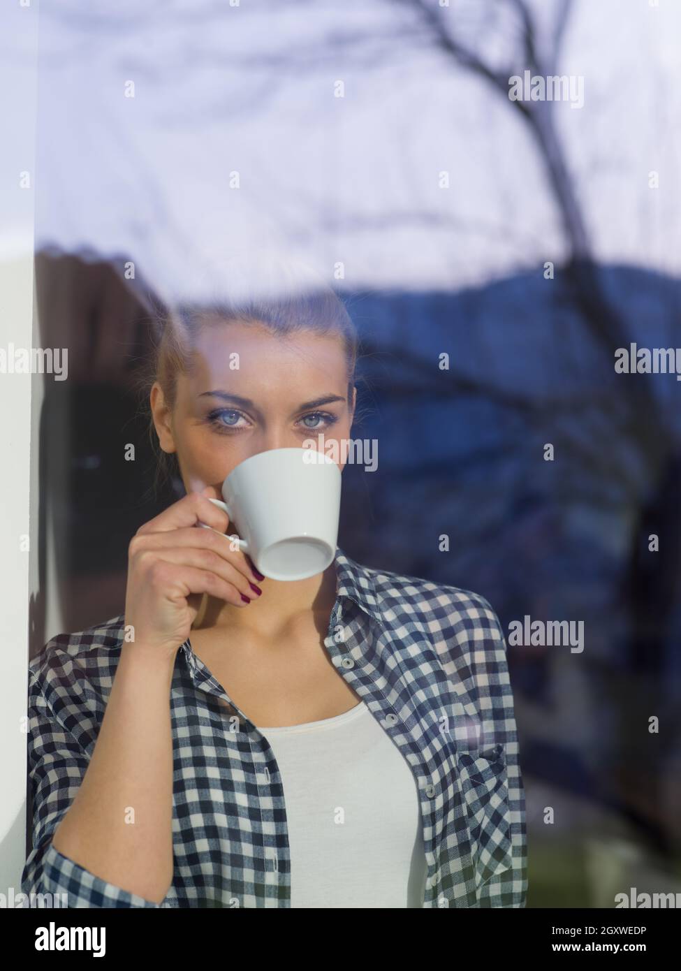 beautiful young woman drinking morning coffee by the window in her home ...