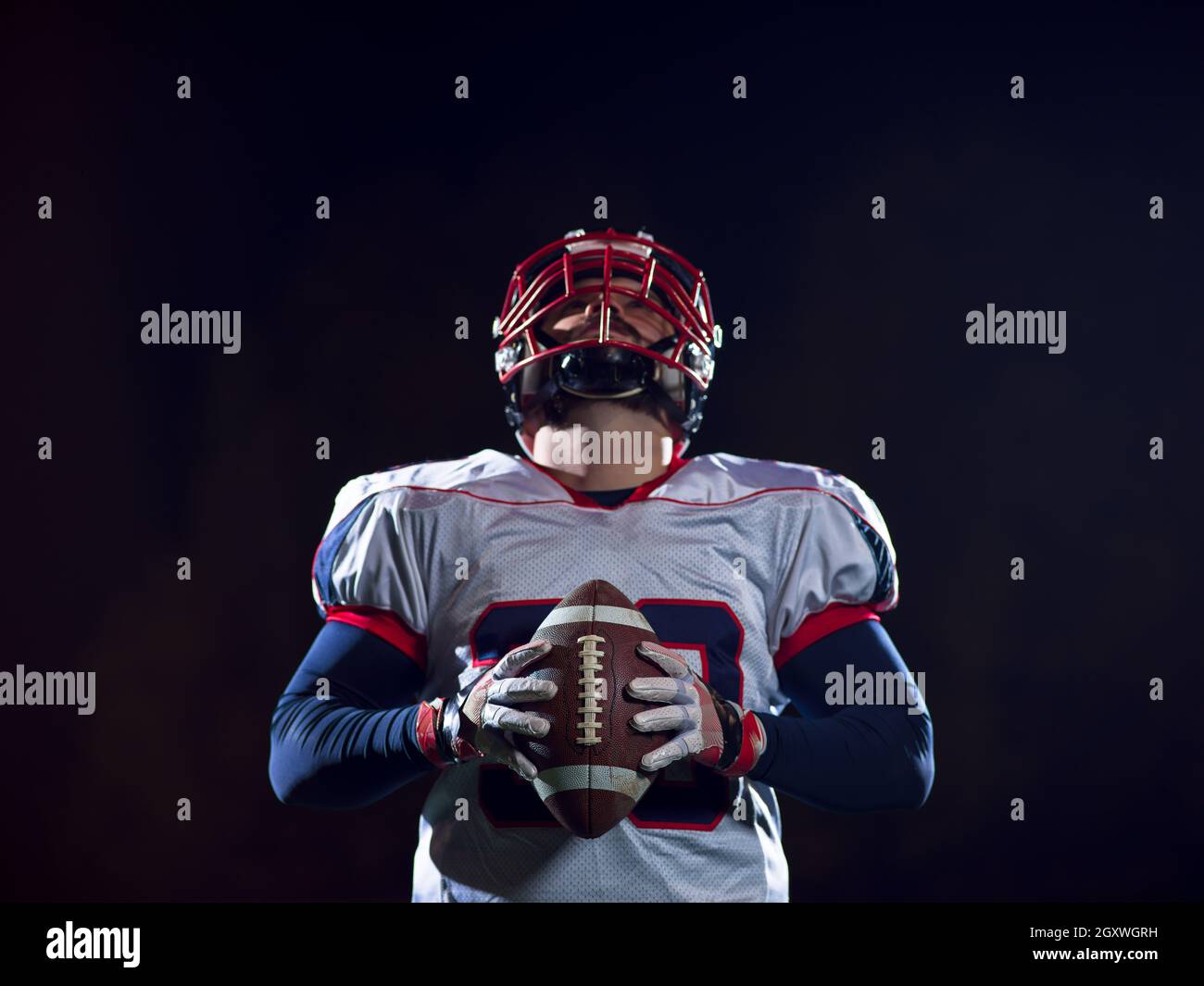 portrait of confident American football player holding ball while ...