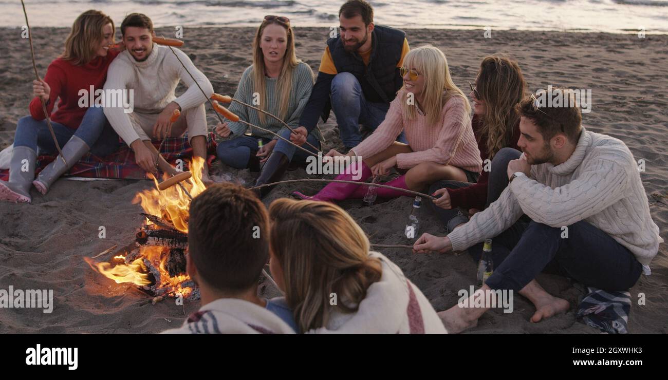 Group of young friends sitting by the fire late at night, grilling ...