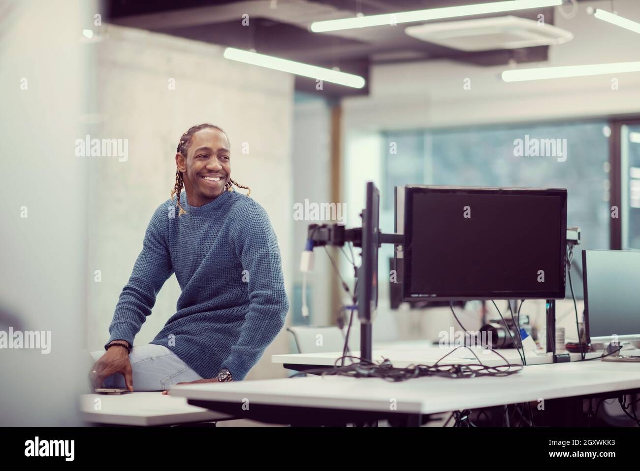 Portrait of young smiling african american male software developer sitting on office desk at ...