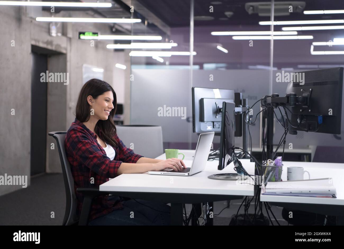 young female software developer using laptop computer while writing programming code at modern ...