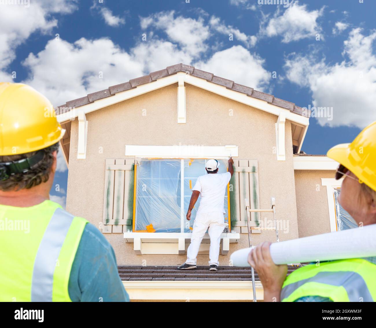 Male and Female Contractors Overlooking Painter Painting House Stock ...