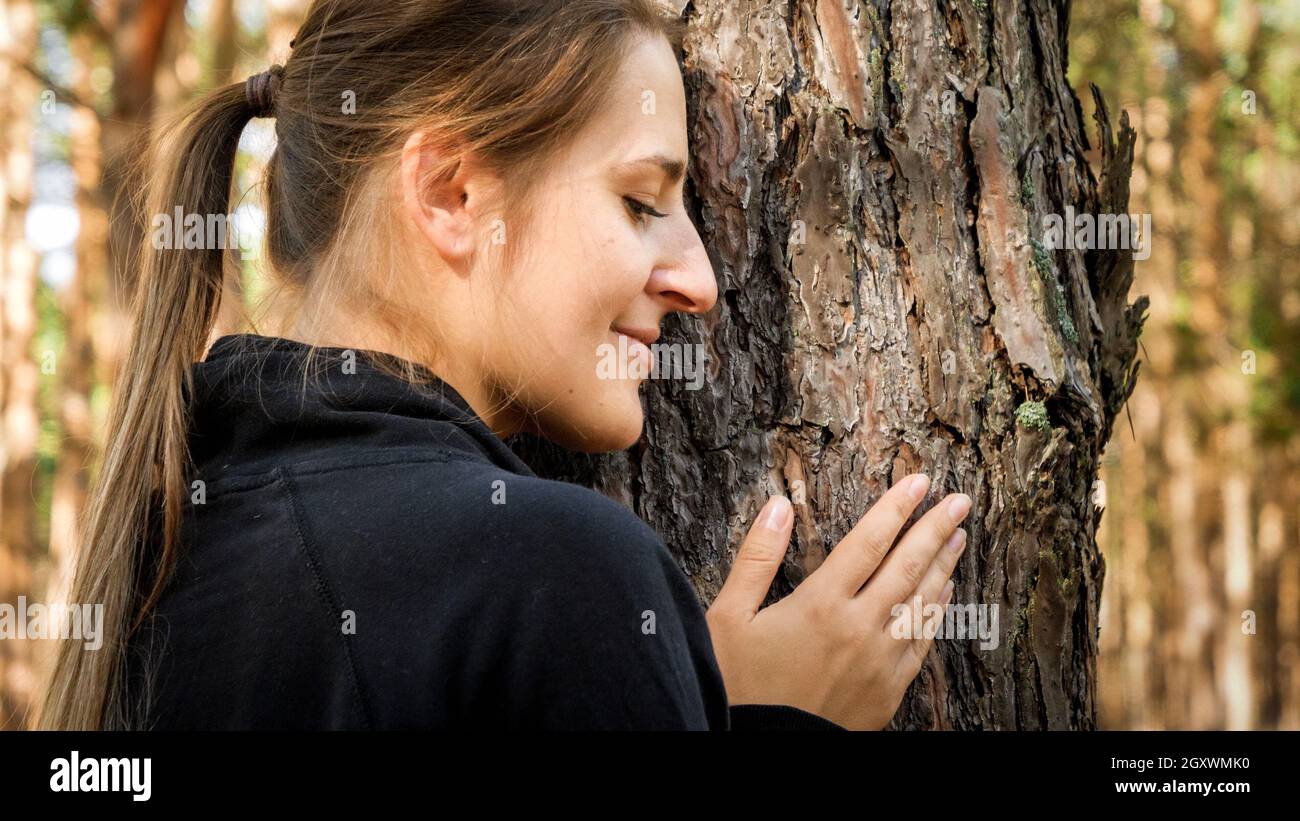 Portrait of beautiful woman leaning and touching old tree in forest ...