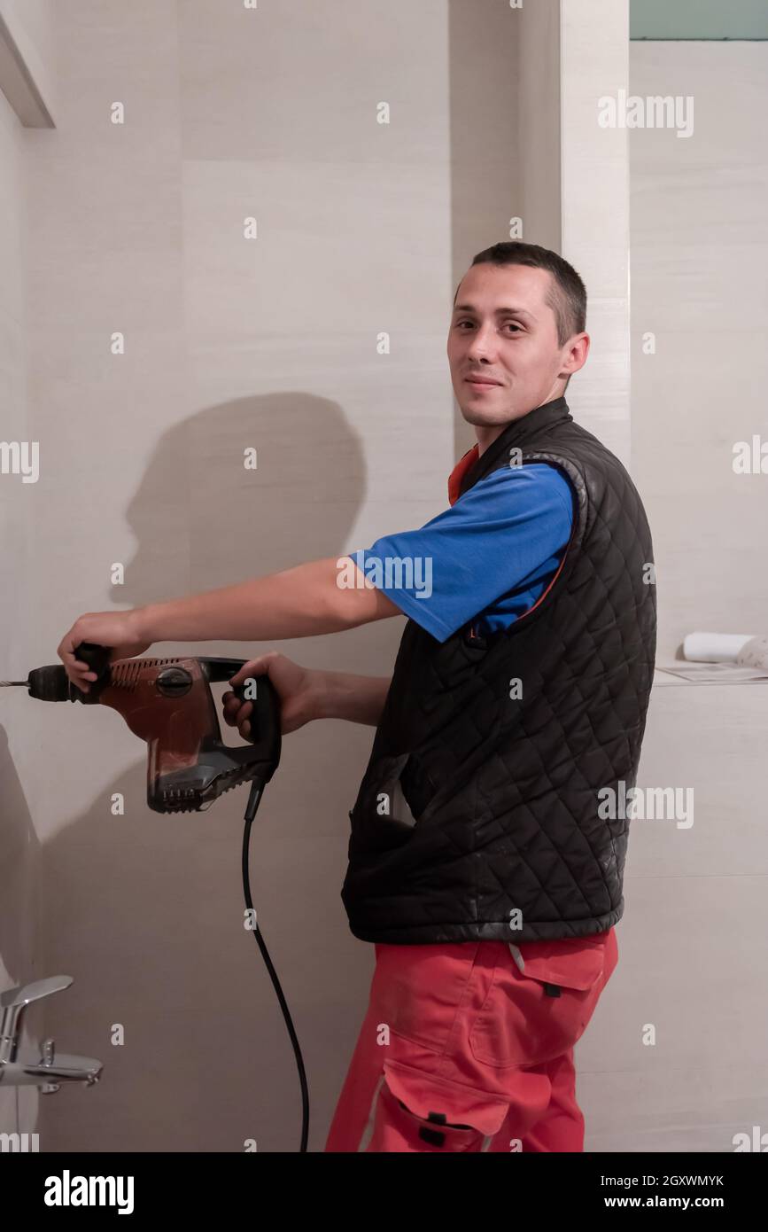 young professional construction worker drilling holes in the bathroom ...