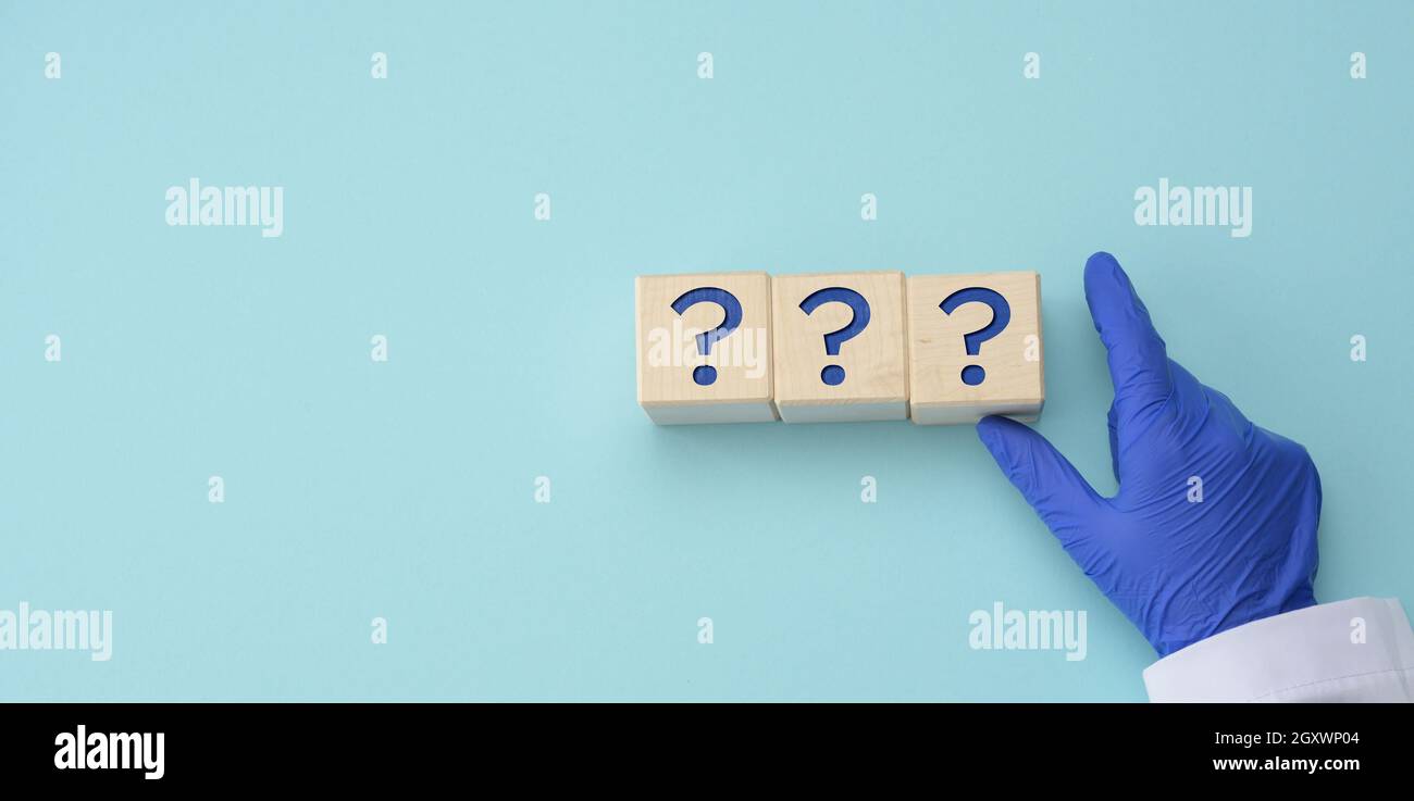 a hand in a blue medical glove holds cubes with question marks on a ...