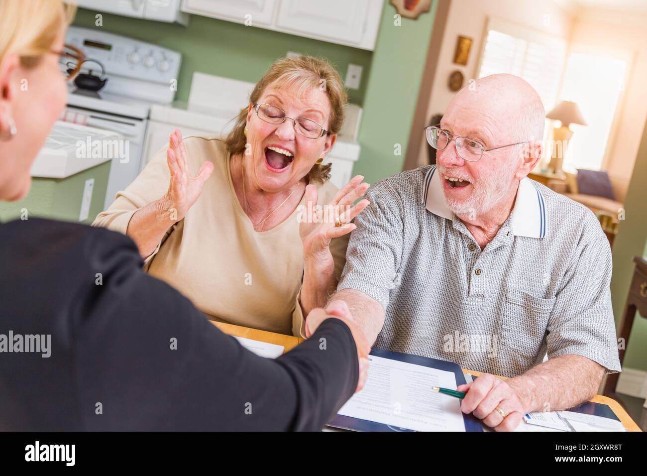 Senior Adult Couple Celebrating Over Documents in Their Home with Agent ...