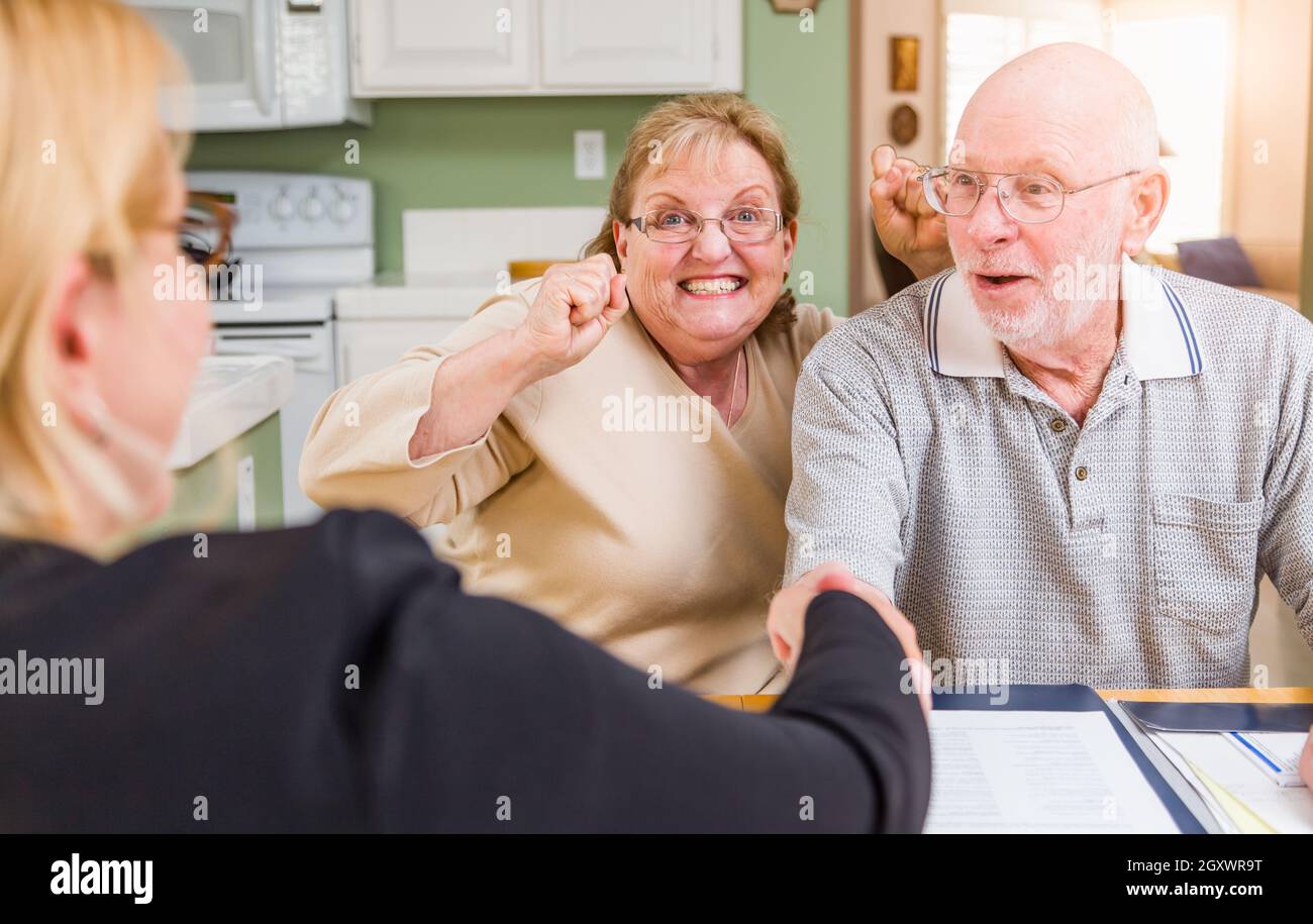 Senior Adult Couple Celebrating Over Documents in Their Home with Agent ...