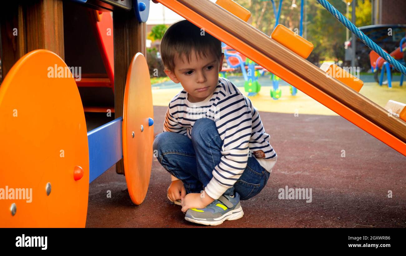 Sad little boy hiding under slide on children playground at ...