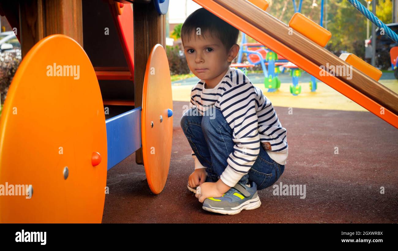 Portrait of sad crying boy sitting under slide on children playground ...