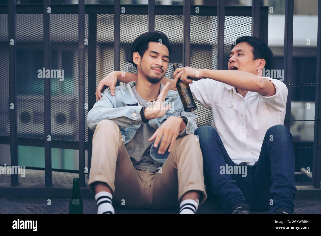 Drunk bearded young man and friend sitting on the street sidewalk after drinking lots of beer ...
