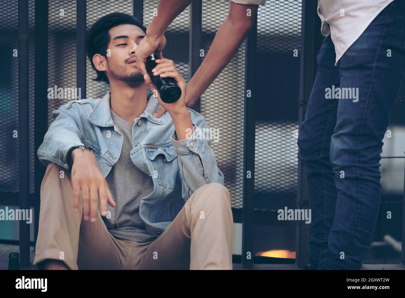 Drunk bearded young man and friend sitting on the street sidewalk after drinking lots of beer ...