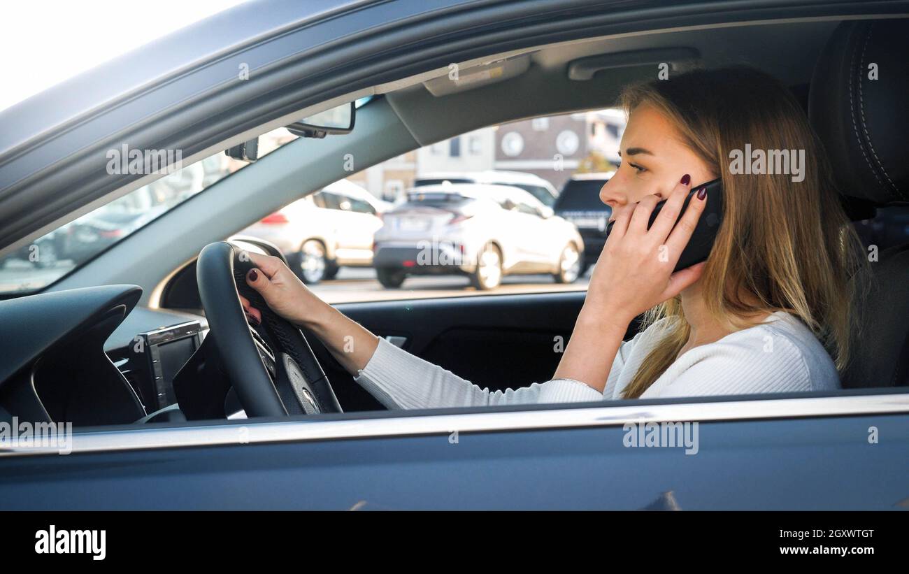 Portrait of irresponsible female driver talking by phone while driving ...
