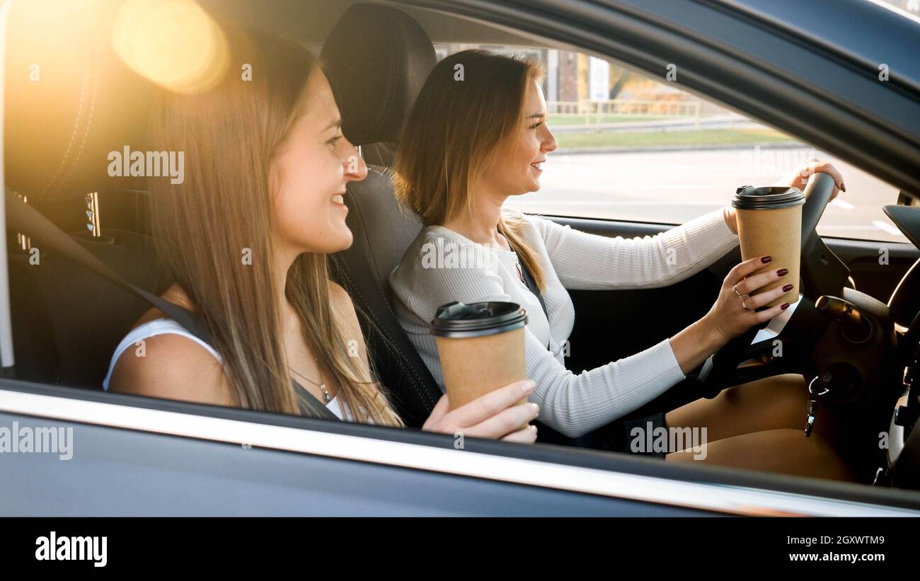 Portrait of two happy smiling girls drinking coffee while riding in car ...