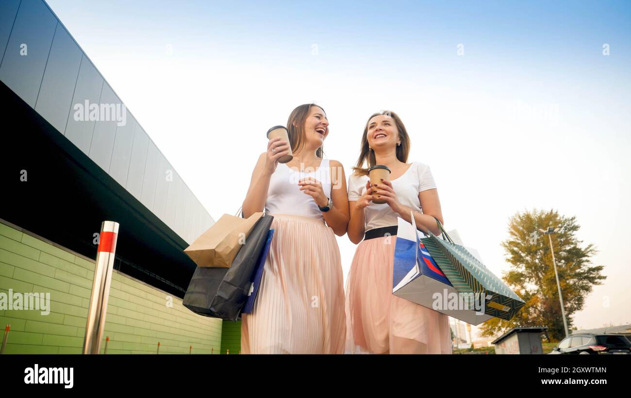 Two happy smiling girls with paper bags walking on street after doing ...