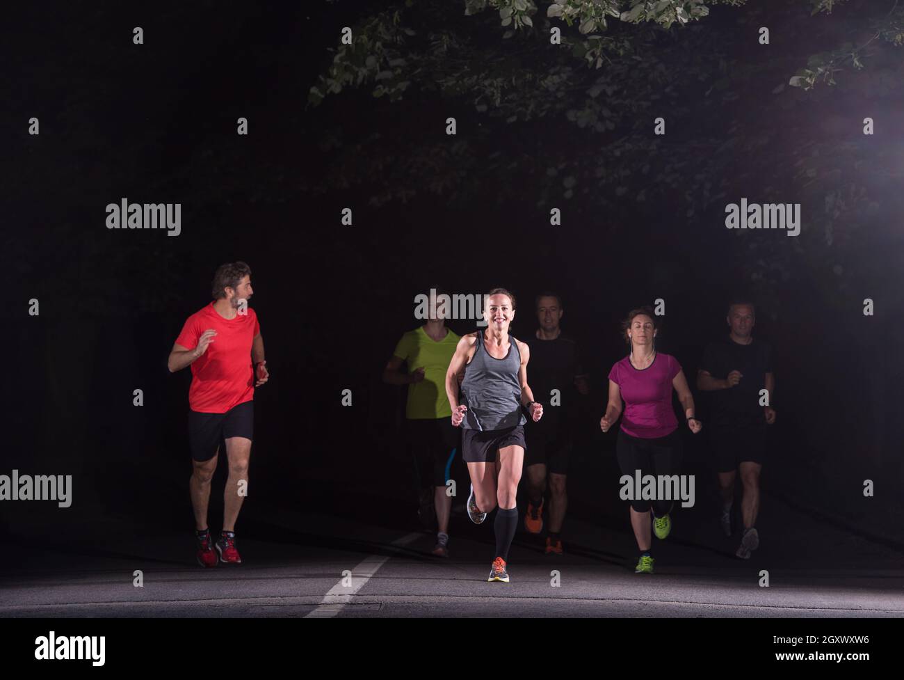 group of healthy people jogging in city park, runners team at night ...