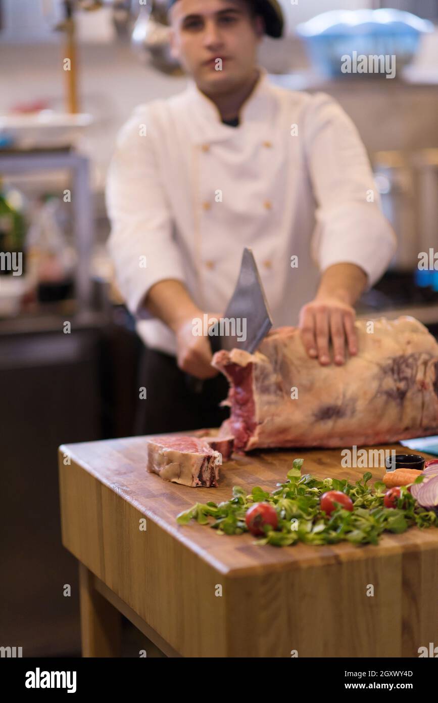 chef using ax while cutting big piece of beef on wooden board in ...
