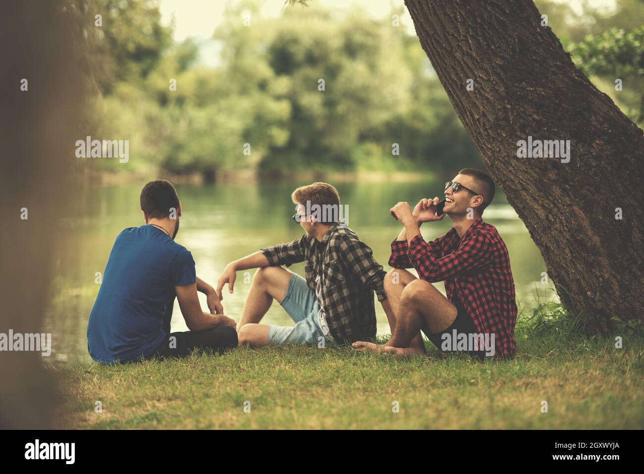 Group of young men enjoying the nature sitting on the bank of the river ...