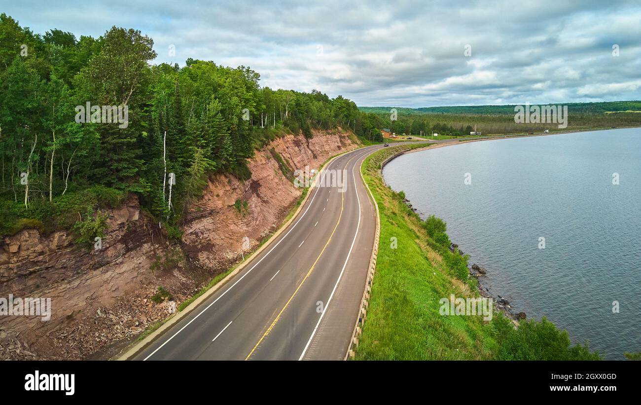 Aerial view over road going around lake and against rocky cliff edge ...