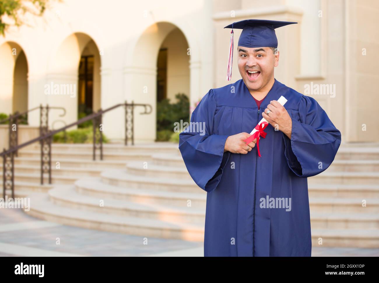 Hispanic Male With Deploma Wearing Graduation Cap and Gown On Campus ...