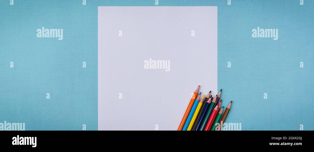 A blank white sheet and colored pencils for drawing on a plain textured ...