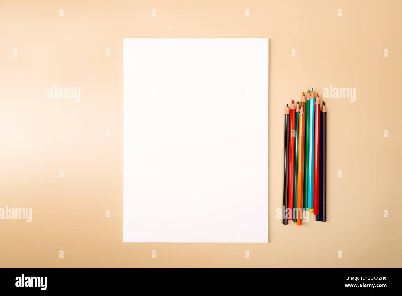 A blank white sheet and colored pencils for drawing on a plain textured ...