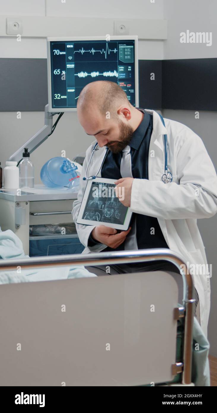 Medic pointing at tablet display with radiography for ill woman in bed ...