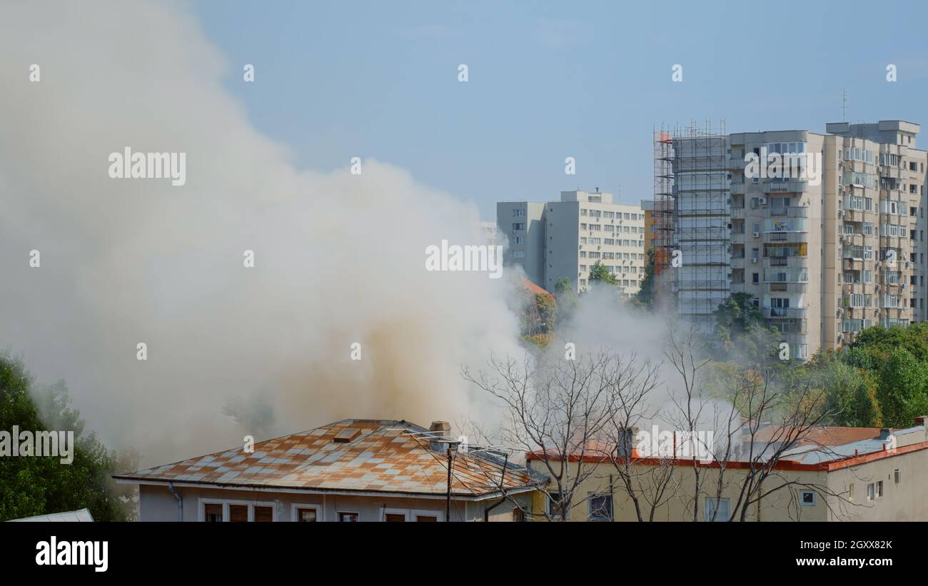 View of flames getting out of burning house in city landscape. Fumes ...