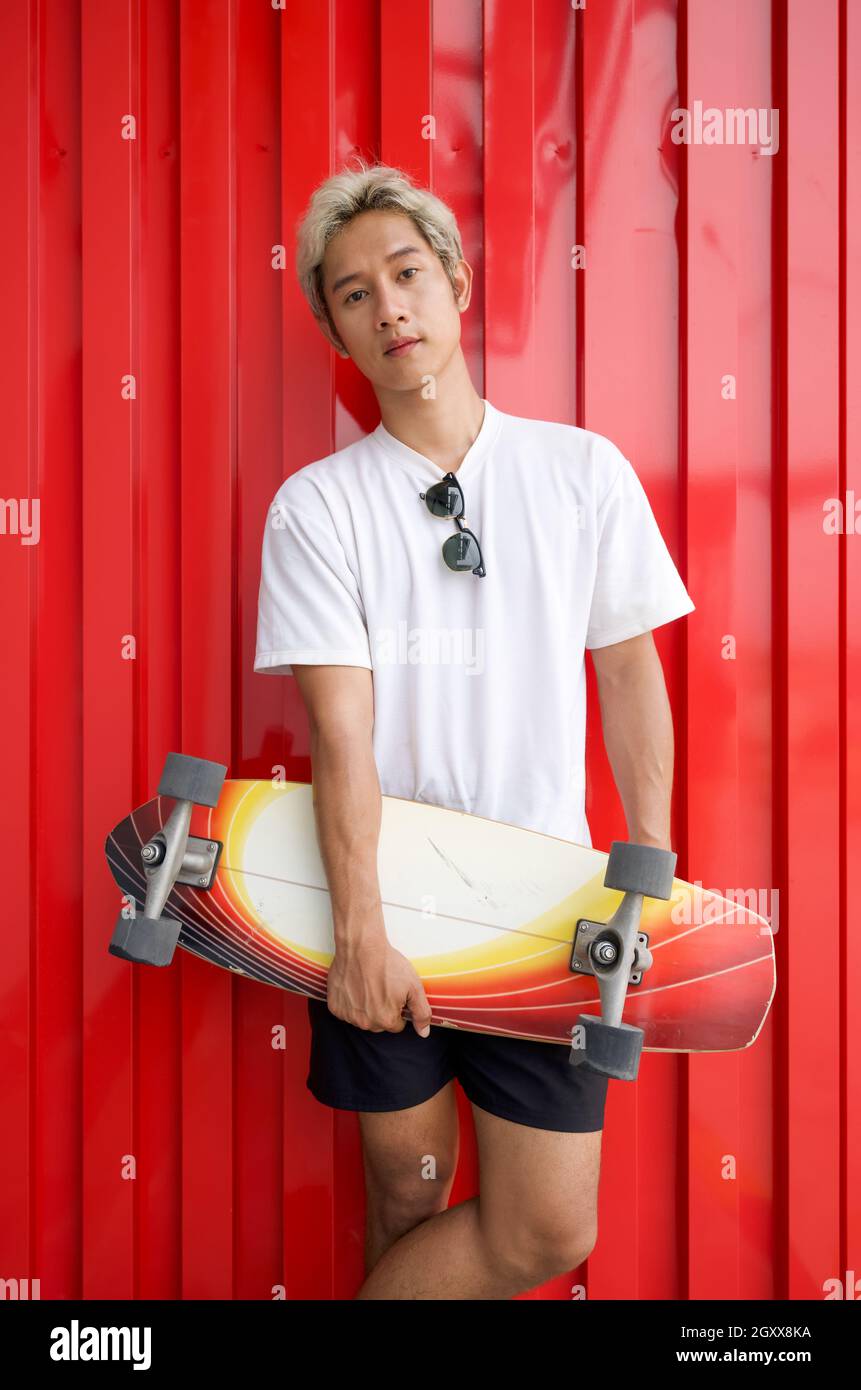 Young asian man in white T-shirt and sunglass holding the surfskate ...
