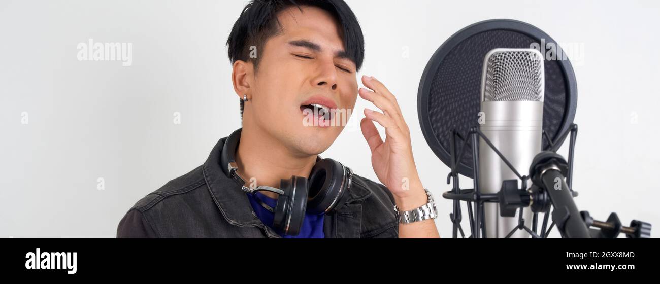 Young asian man with headphones singing with microphone. Portrait on ...