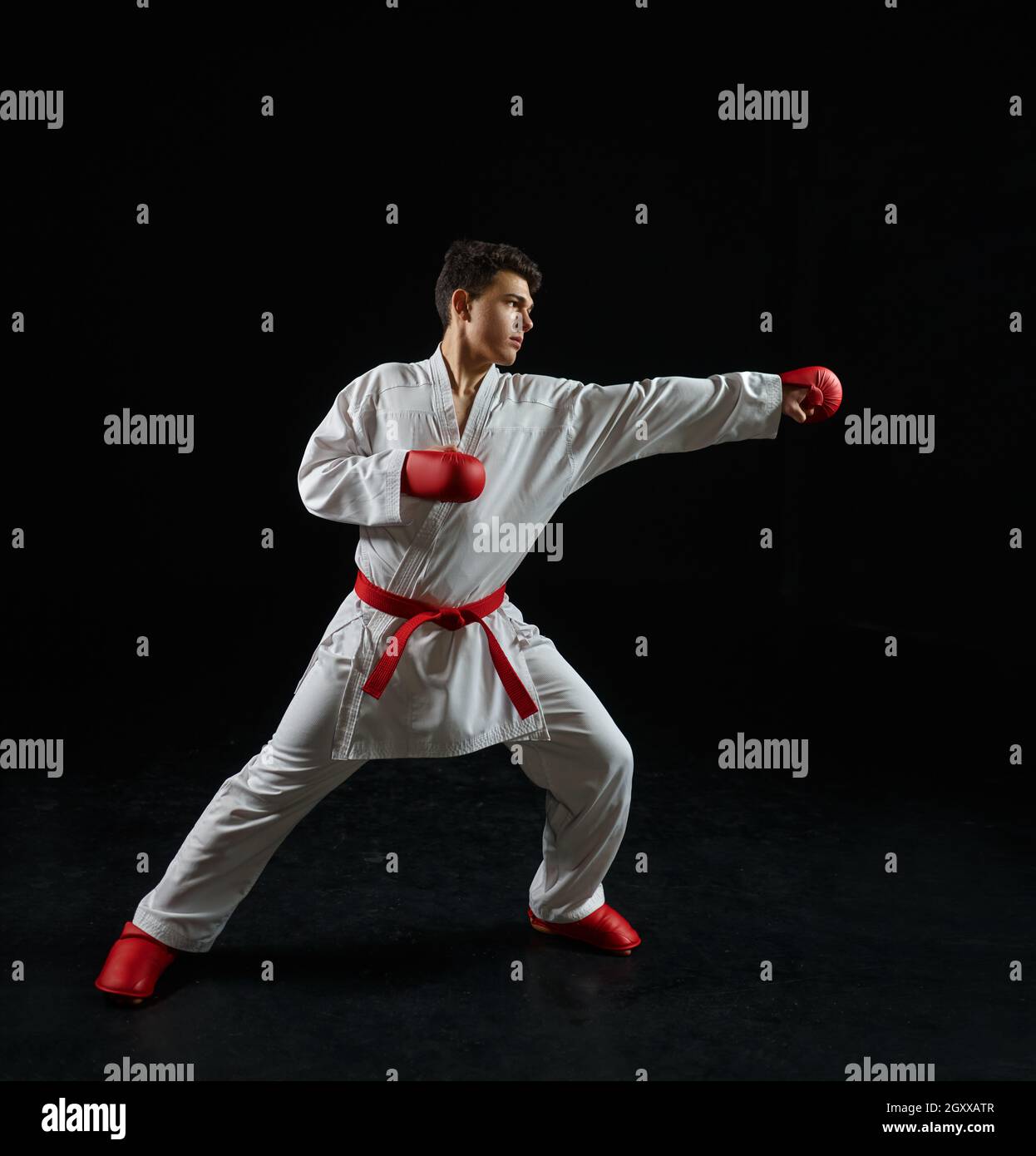 Male karate fighter in white kimono and red gloves, combat stance, dark ...