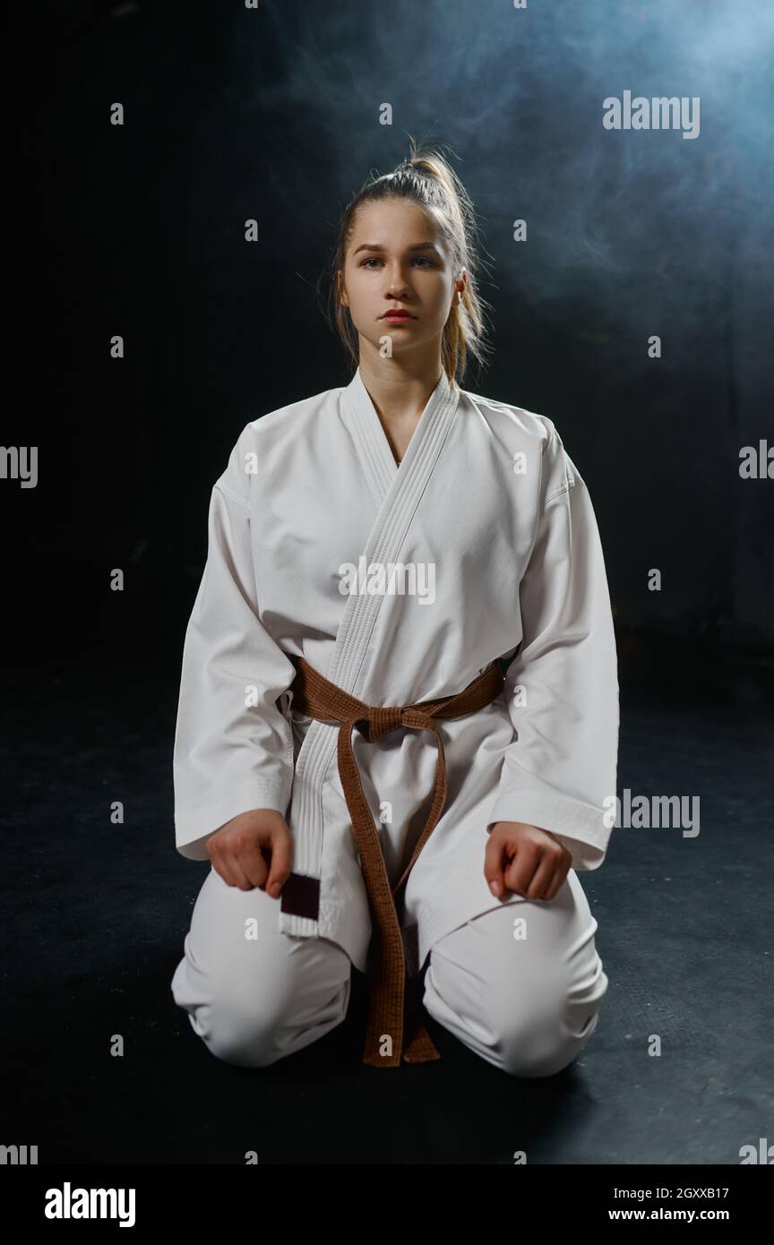 Female karateka on training in white kimono sitting on the floor, dark ...