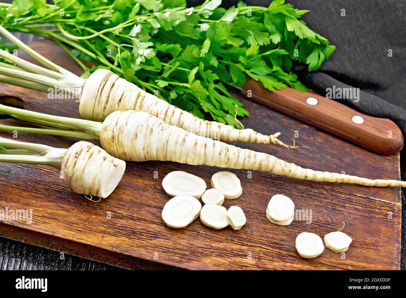 Parsley roots whole and chopped with green tops, knife, napkin on the ...