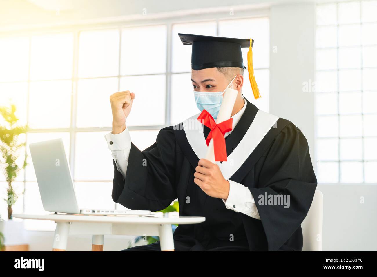 Happy graduation wearing medical mask and watching the laptop, holding ...