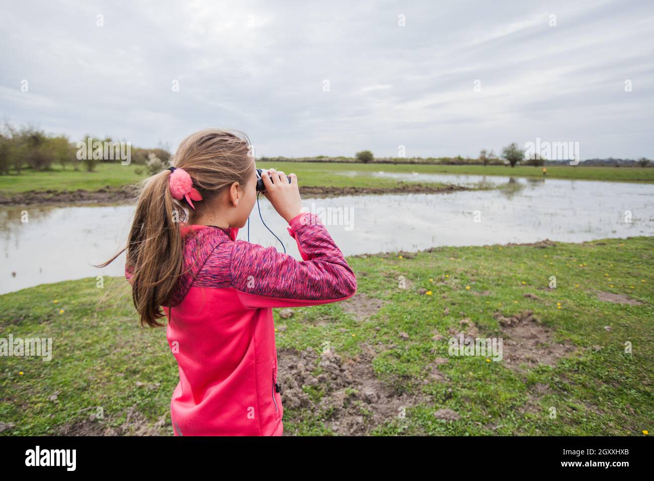 Little girl observing with binoculars nature landscape on cloudy spring ...