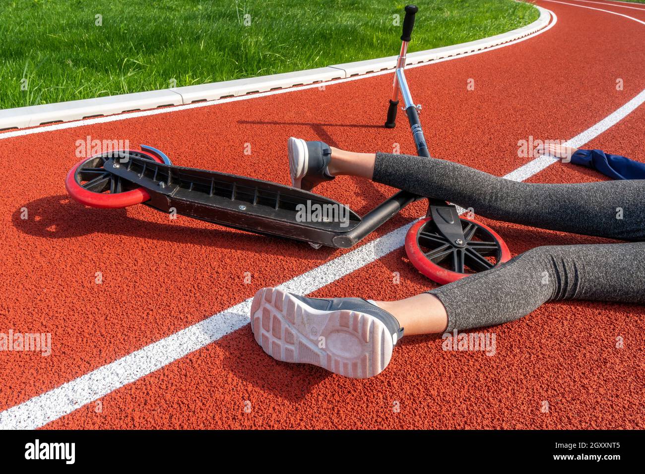 Girl lying on the ground after falling off her scooter. Child getting ...