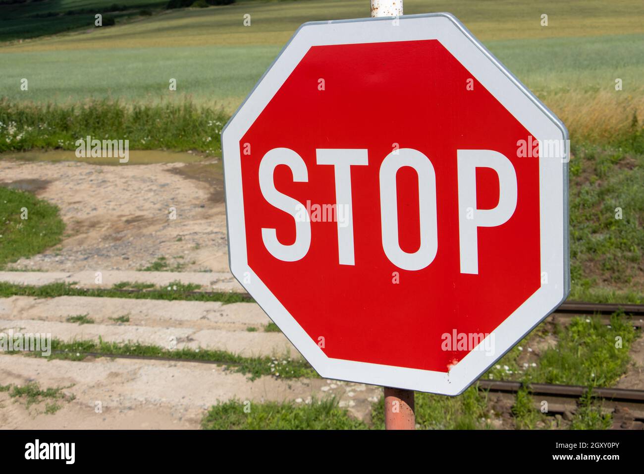 A red sign STOP before crossing the tracks with a field road, close up ...