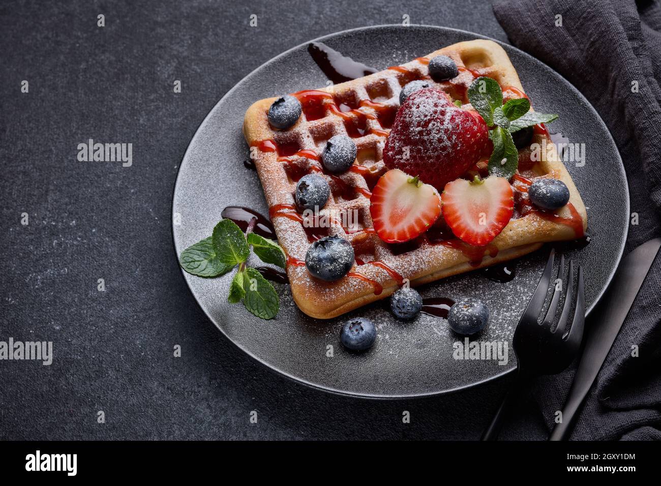 Delicious waffles with berries, mint, powdered sugar and sweet sauce on ...